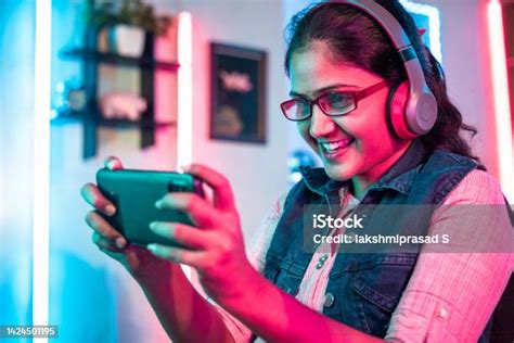 집에서 휴대 전화에서 온라인 비디오 게임을하는 헤드폰과 안경을 가진 행복한 웃는 소녀 라이브 스트리머 거룩한 날과 사이버 공간의 개념 인도 인도아 대륙에 대한 스톡 사진 및
