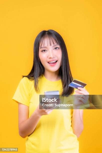 아름다운 아시아 젊은 여자 귀여운 여자 앞머리 헤어 스타일 노란색 셔츠에 신용 카드와 스마트 폰을 들고 휴대 전화는 노란색 배경에 고립 된 온라인 쇼핑을 지불하기 위해