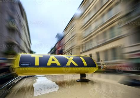 A Taxi Sign On A Car With A Lot Of Motion Blur On The City Background