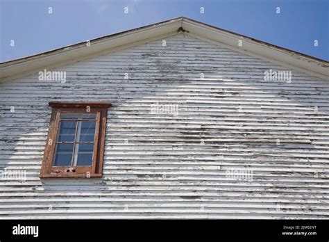 Brown Window And Peeling White Paint Clapboard Cladding On Side Wall Of