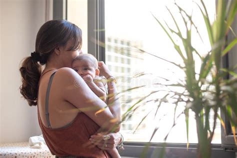 Woman Looks Out The Window Of Her Home While Holding Her Newborn Daughter Stock Image Image Of