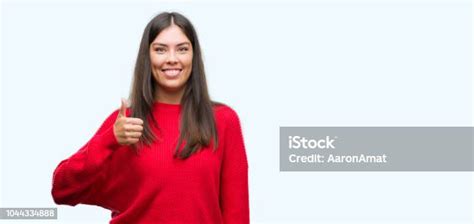 젊은 아름 다운 히스패닉 행복 엄지손가락 손으로 제스처를 하 고 빨간 스웨터를 입고 승인 성공을 보여주는 카메라를 보고 하는 식 겨울에 대한 스톡 사진 및 기타 이미지