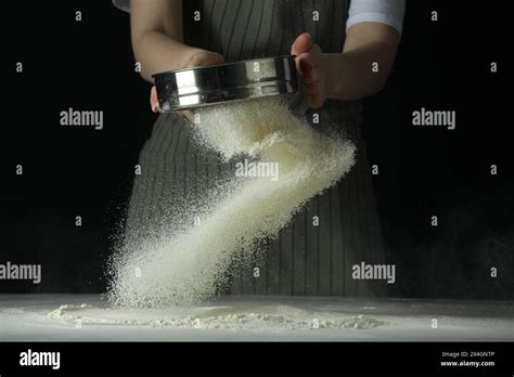 Woman Sieving Flour At Table Against Black Background Closeup Stock