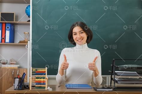 工具高清图片 微笑着看着相机，镜头里显示年轻女老师坐在课桌前，教室里放着学校工具，竖起大拇指 教育文化免费下载格式626像素编号53629339 千图网