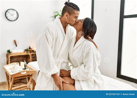 Young Latin Couple Wearing Bathrobe Kissing And Sitting On Massage