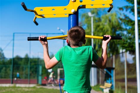 Boy Doing Pull Ups On Outdoor Fitness Equipment Sunny Day Active