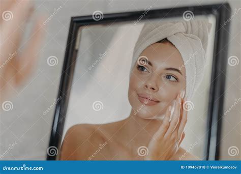Young Naked European Woman Touches Soft Skin On Face Looks At Herself