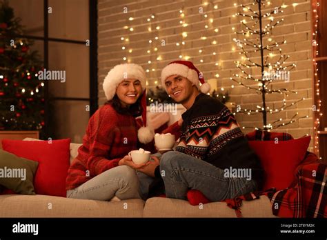 Young Couple Drinking Hot Cocoa With Marshmallows On Sofa At Christmas