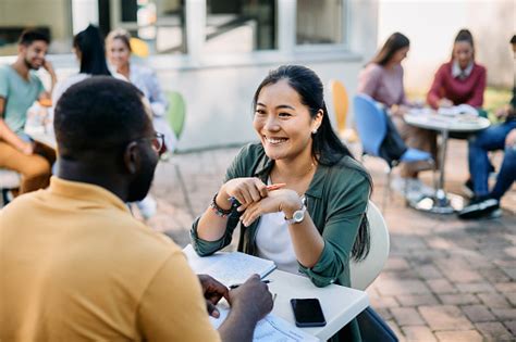 Happy Asian Student And Her Black Classmate Talking While Studying At