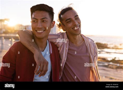Happy Biracial Gay Male Couple Walking And Embracing On Promenade By