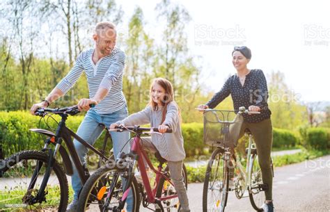여름 야외 자전거를 타는 동안 딸과 함께 웃고 있는 아버지와 어머니 그들은 여름 도시 공원에서 함께 시간을 즐깁니다 행복한 부모와 어린 시절 또는 활동적인 스포츠 생활 개념