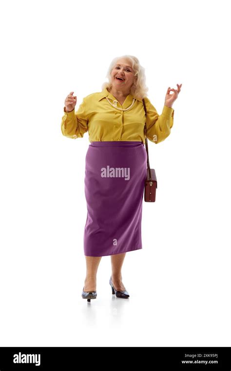 Joyful Elderly Woman In Bright Yellow Blouse And Purple Skirt Stands