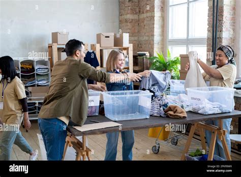 Happy Females Choosing Donation Clothes From Containers On Table Stock