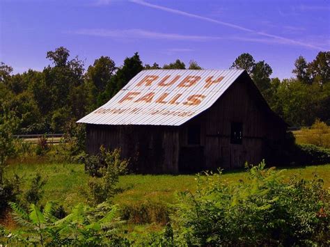 An Old Rusted Metal Sign On The Side Of A Building In A Field With Trees