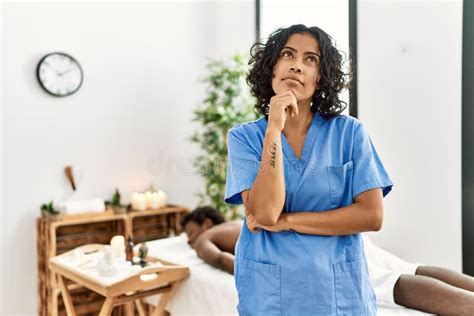 Young Therapist Woman At Wellness Spa Center With Hand On Chin Thinking