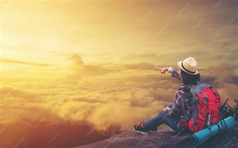 Side View Of Hiker Pointing While Sitting On Cliff Against Sky During