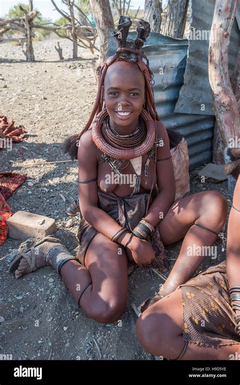 A Young Girl In Traditional Clothes And Decoration From Himba People Is Sitting And Trading At