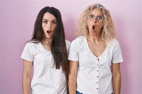 Mother And Daughter Standing Together Over Pink Background In Shock