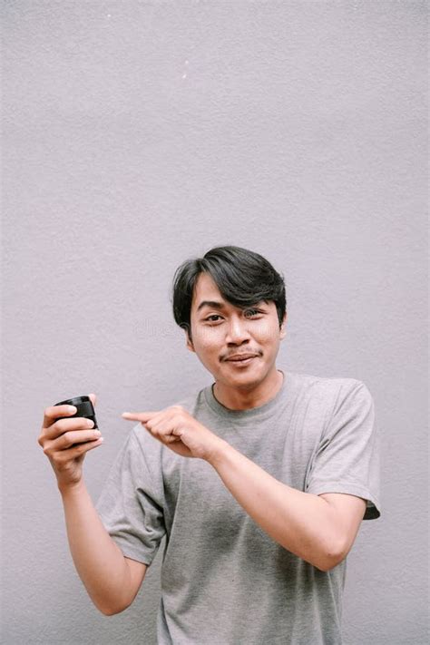 Young Asian Man Pointing Finger Holding Black Jar Presenting Product