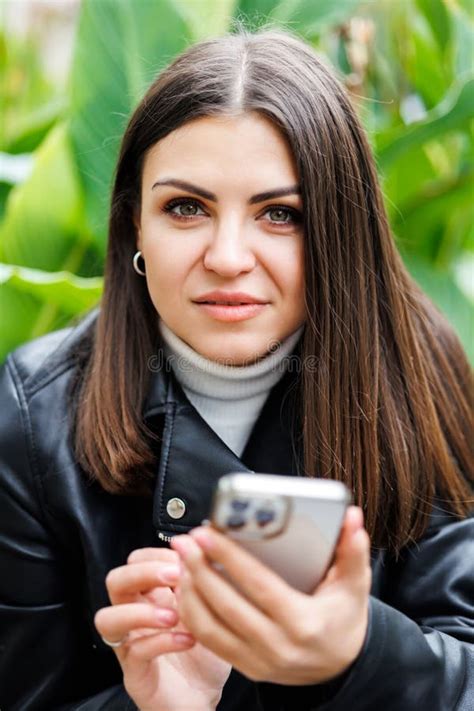 Una Jovencita Linda Con Una Chaqueta De Cuero Negro Camina Por La Calle En Un Parque Y Usa Su