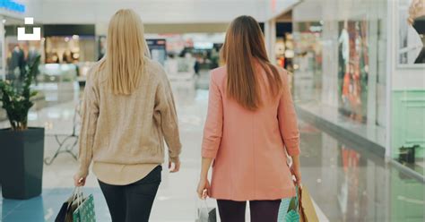 Two Women Walking In A Brightly Lit Shopping Mall Photo Free
