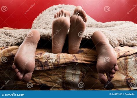 Two Pairs Of Male And Female Feet Seen From Under The Blanket Sleep