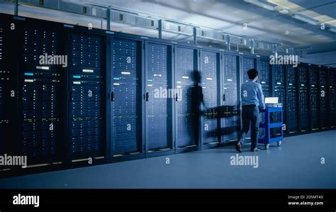 In The Modern Data Center It Engineer Doing Maintenance And Diagnostics Pushes Cart Alongside