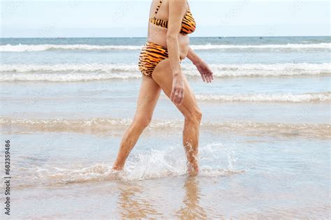 Barefoot Senior Woman Walking Along The Beach Shore Dipping Her Feet In