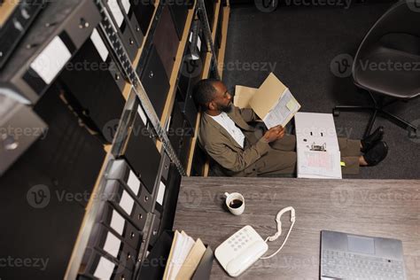 Detective Sitting On Office Floor Searching Csi Report In Folder At