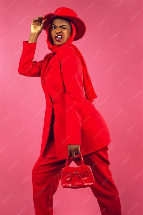 Premium Photo A Woman In A Red Suit Holding A Hat Is Tilted To Her Mouth Looking At The Camera