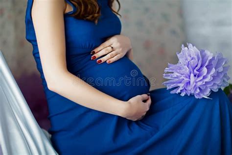 Young Pregnant Woman In A Blue Dress Holds Her Hands On Her Swollen