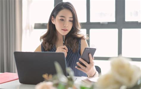 Concentrated Young Beautiful Asian Sitting At Desk With Laptop Computer