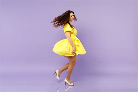 여름 노란색 드레스에 쾌활 한 젊은 여자는 스튜디오에서 파스텔 바이올렛 배경에 고립 옆으로 찾고 머리를 끼고 소용돌이 사람들은