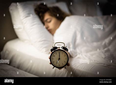 Alarm Clock On The Bed With Sleeping Woman Behind Girl Keeps Alarm Clock By Her Hand Stock