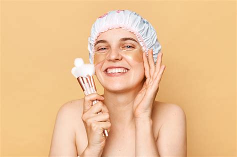 파우더 브러쉬를 들고 화장을 하는 기쁜 아름다운 여성이 베이지색 배경 위에 고립된 눈 아래에 패치를 들고 행복하게 웃고 있다 30 34세에 대한 스톡 사진 및 기타 이미지