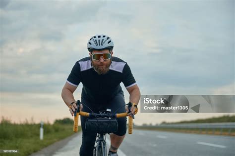 젊은 수염 난 남자의 역동적인 이미지 저녁에 텅 빈 도로에서 자전거를 타는 헬멧을 쓴 자전거 타는 사람 농도 25 29세에 대한