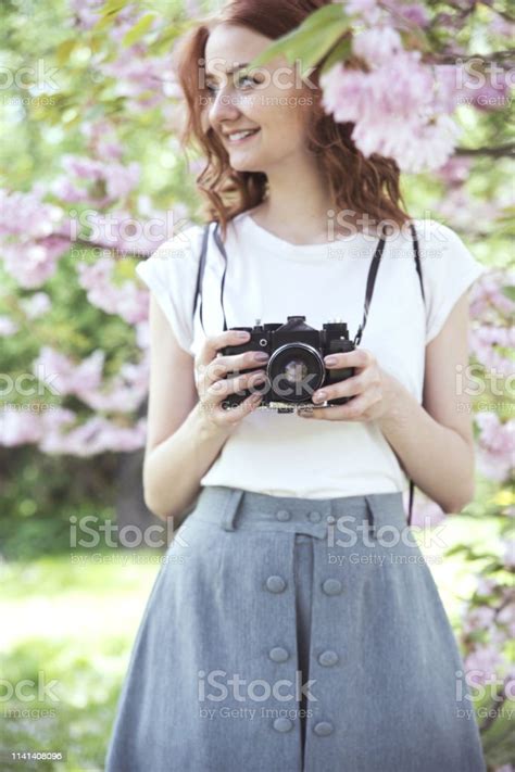 흰색 T 셔츠와 회색 치마에 젊은 아름 다운 빨간 머리 소녀 봄 꽃 벚꽃 나무 정원에서 사진을 촬영 합니다 취미 블로그 블로거 아날로그 사진 소셜 미디어 산책을 위한 봄