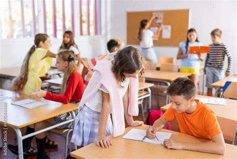 Positive Friendly Tween Girl Helping Classmate Sitting At School Desk