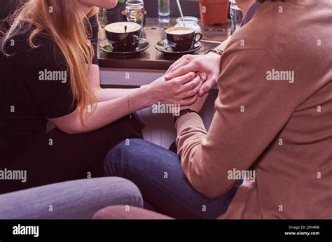 Close Up Of A Young Couple Holding Hands Together Sitting In Cafe Stock