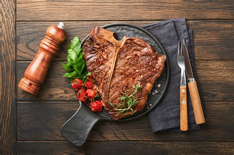 스테이크 티본 얇게 썬 쇠고기 구운 Tbone 또는 포터 하우스 고기 스테이크와 향신료 로즈마리와 후추는 오래 된 나무 배경에 검은 대리석 보드에 있습니다 평면도 모의 0