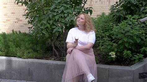 A Plump Caucasian Woman Eats An Ice Cream Cone While Walking Stock