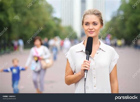 خبرنگار جوان با میکروفون در دست در خیابان ایستاده و به دور نگاه می کند