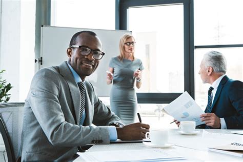 젊은 아프리카계 미국인 사업가 메모 및 비즈니스 회의에서 동료 들과 대화를 나누는 동안 카메라에 웃 고 기업 비즈니스에 대한 스톡 사진 및 기타 이미지 Istock