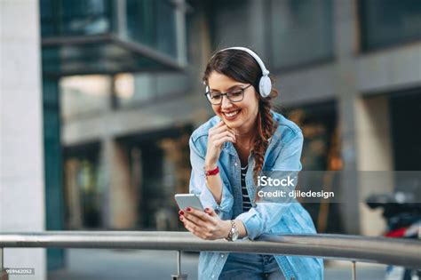 젊은 여자는 도시에 스마트폰 및 헤드폰을 통해 영상 통화를 만들기 도시에 대한 스톡 사진 및 기타 이미지 도시 명랑한