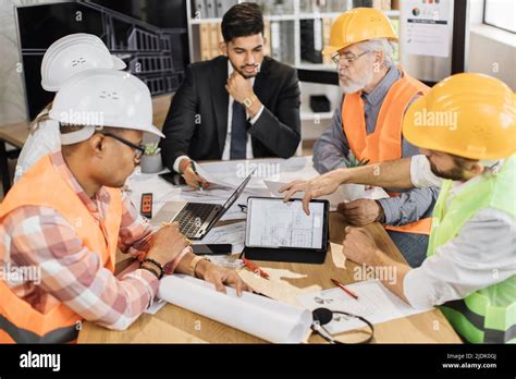 Construction Team Analysing Blueprints During Business Meeting At