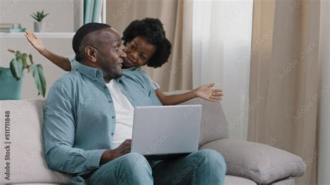 Adult Male Freelancer Sits In Room On Couch Working Remote On Laptop