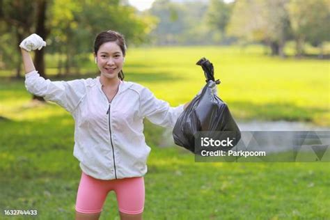 아침 달리기 후 젊은 아름다운 아시아 자원 봉사 여성은 쓰레기 봉투를 들고 공원 잔디밭에서 쓰레기를 줍고 자원 봉사 환경 청소 중에 플라스틱 병과 전체 검은색 가방을 보여