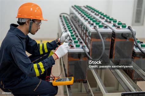 산업 환경에서 멀티미터로 배터리 유지 보수를 수행하는 기술자 안전 장비에는 헬멧과 장갑이 포함되어 안전한 환경을 보장합니다 전기 연료 및 전력 생산에 대한 스톡 사진 및