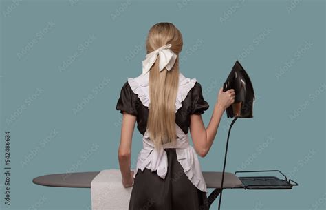 A Woman Dressed As A Maid Irons A Towel On An Ironing Board Back View