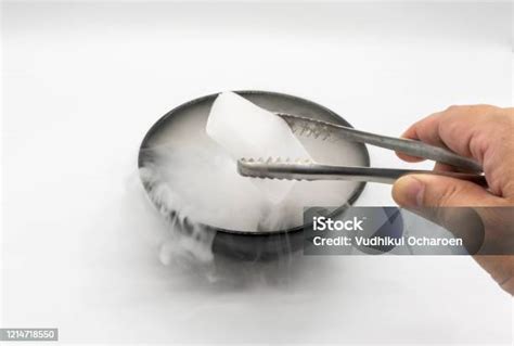 흰색 배경에 고립 된 움직임에 연기가 자욱한 흰색의 검은 그릇 위에 드라이 아이스와 얼음 트위저를 들고 손 드라이아이스에 대한